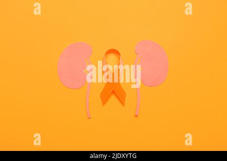 Orange ribbon and paper kidneys on color background. Cancer awareness ...