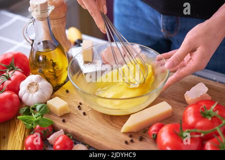 Woman beating egg yolks with a whisk making homemade pasta carbonara ...