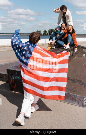 Young woman with USA flag pointing at viewer on blue background ...