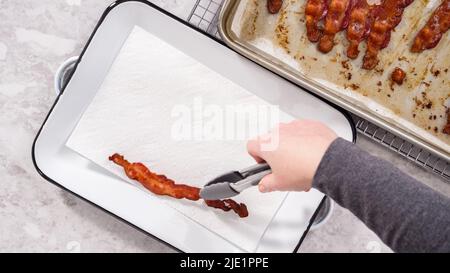 Step by step. Cooked bacon strips on a white tray with a paper towel ...