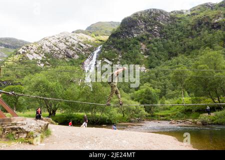 Man walking across Steall wire bridge over Water of Nevis river with ...