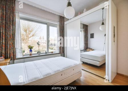 Comfortable bed next to a bright window and wooden floor Stock Photo ...