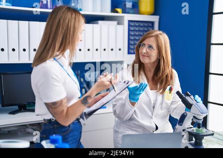Mother and daughter scientists writing on document using microscope at ...
