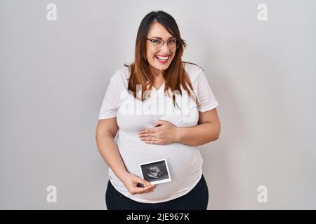 Pregnant woman holding baby ecography relaxed with serious expression ...