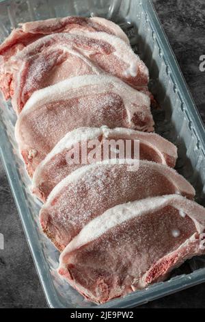 Frozen pork chops in plastic tray packaging thawing. On a concrete ...