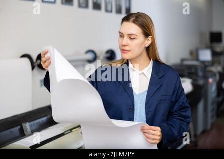 Printing establishment worker examining large piece of paper Stock ...