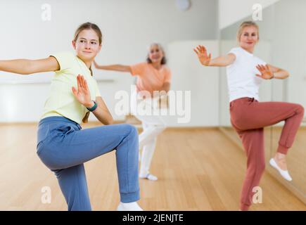 Teen girl with family exercising dance moves with group of people in ...