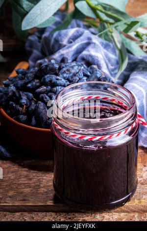 Small glass jar with homemade haskap berry jam, on wooden background ...
