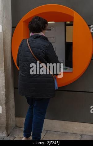 Young adult woman withdrawing money from an ATM cash machine outdoors ...