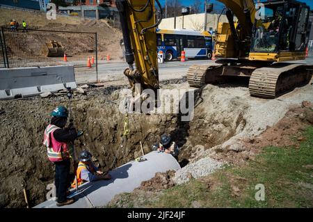 An excavator stands by after placing a section of concrete sewer pipe ...