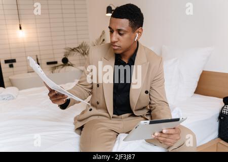 Black man working with papers and tablet computer while sitting on bad ...