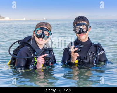 Smiling scuba divers in the sea, facing the camera with their dive ...