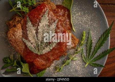 Marijuana butter cake with sugar plum and medicinal herbs on blue plate ...