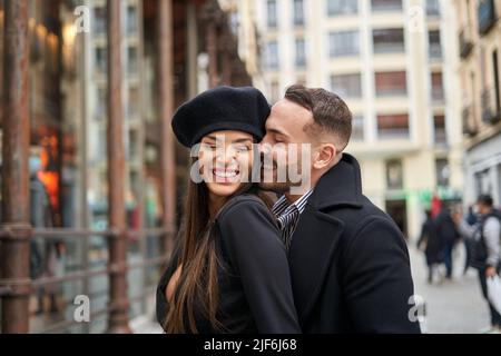 Positive couple in outerwear caressing while standing looking at each ...