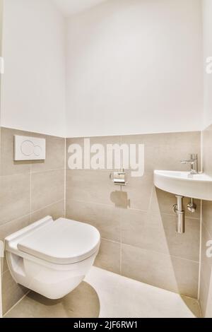 Wall hung toilet and small sink in corner in lavatory room with beige ...