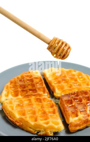 Soft muffin waffles poured with fresh honey using honey spoon, in plate ...