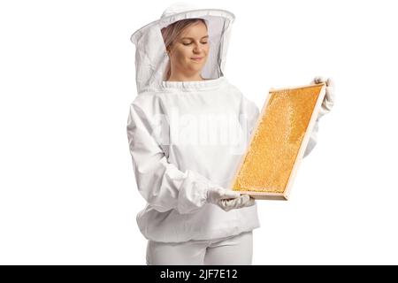 Young female bee keeper in a uniform leaning on a honeycomb frame and ...