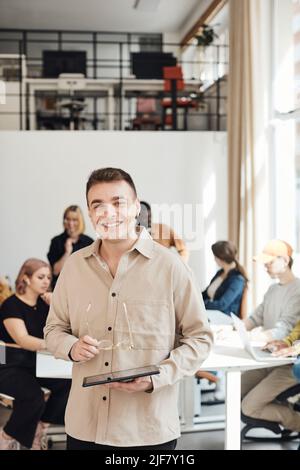 Portrait of smiling male programmer holding tablet PC while standing in ...