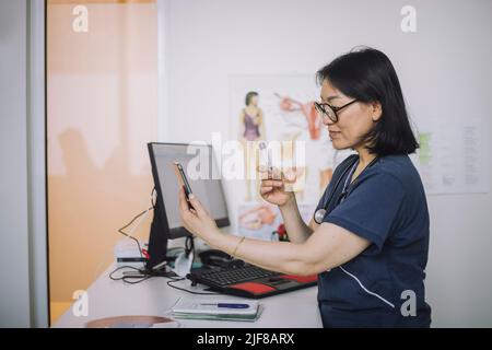 Mature doctor in eyeglasses doing vaccination of man on blurred ...