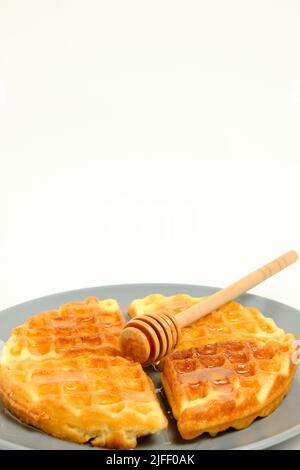 Soft muffin waffles poured with fresh honey using honey spoon, in plate ...