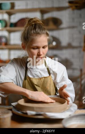 A ceramist makes a plate. Woman in an apron works in a pottery workshop ...