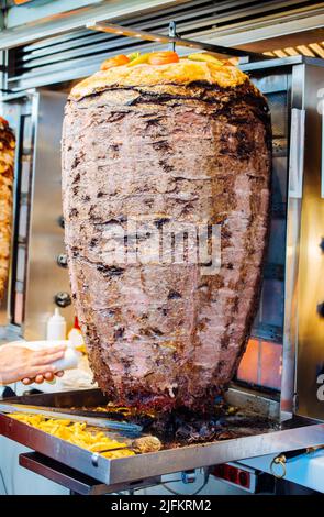 Chef cutting grilled lamb meat from rotating spit making traditional ...