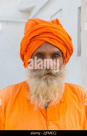 Sadhu in saffron colour garments seating in front of a deity painting ...