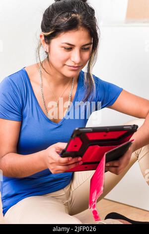Bolivian young Hispanic woman doing school homework with digital tablet ...