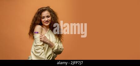 Young woman getting vaccine showing arm with band aid pointing finger ...