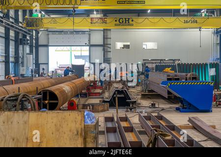 Interior of a steel factory with mobile cranes, steel piles and beams ...