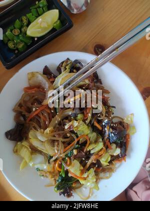 Japchae with carrots and sesame seeds in the white plate on the table ...