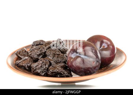 Two fresh black plums and a few prunes on a clay dish, close-up ...