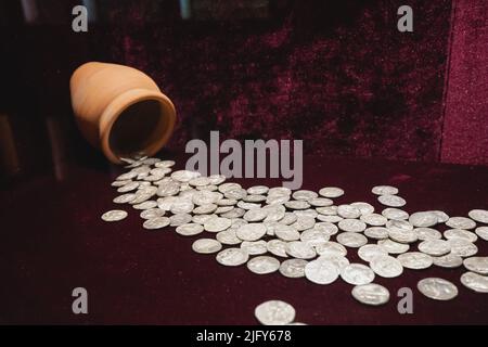 Clay pot with coins. Old Greek coins are scattered on the Plexiglass ...