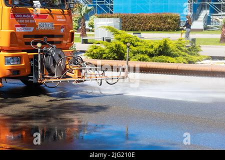 An orange sprinkler washes the asphalt in a spacious spring park on a ...