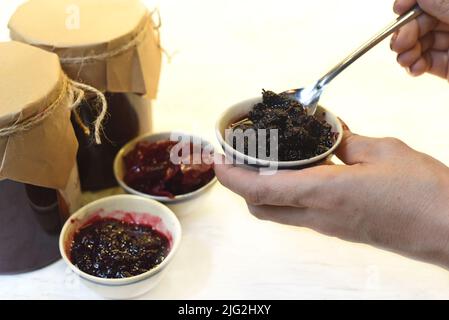 A hand serving homemade mulberry jam in small bowls from jars Stock ...