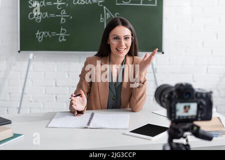 Teacher talking near blurred digital camera and chalkboard with math ...