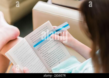 Dyslexic child reading with dyslexia color overlay in his book. A green ...