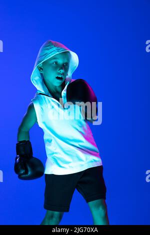 Stylish boy, beginner boxer training isolated over blue background in ...