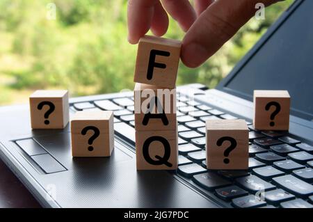 FAQ word on wooden block on top of laptop with blurred nature ...