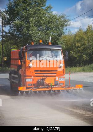 Big orange machine clears the asphalt with a sweeper near the curb ...