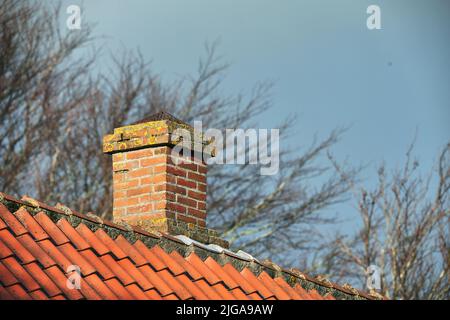 Red brick chimney designed on slate roof of a house building outside ...