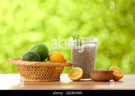 Glass of water with chia seeds, basket and citrus fruits on table ...