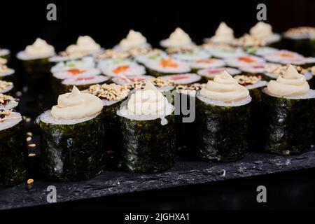 Side view Maki rolls covered with cream cheese lie on a black stone ...