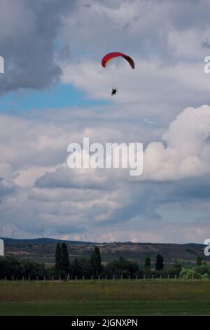Parachutist flying close to ground to land with trees and hills at the ...