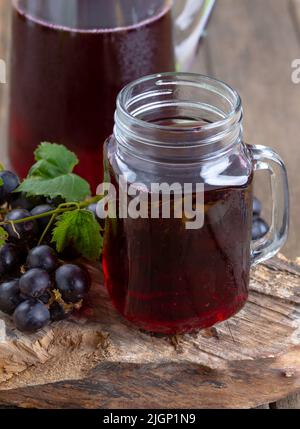 Grape juice in glass and pitcher with red grapes in a basket on wooden ...