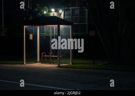 A nighttime shot of a bus stop booth with a red bench Stock Photo - Alamy