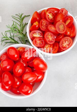 Bowls of small cut and uncut Rosa tomatoes on mottled grey with copy ...
