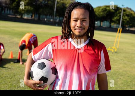 Portrait of biracial smiling male player with dreadlocks holding soccer ...