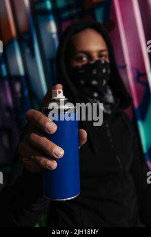 African american vandal holding spray paint near graffiti on wall in ...