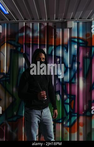African american hooligan with mask on face holding baseball bat in ...